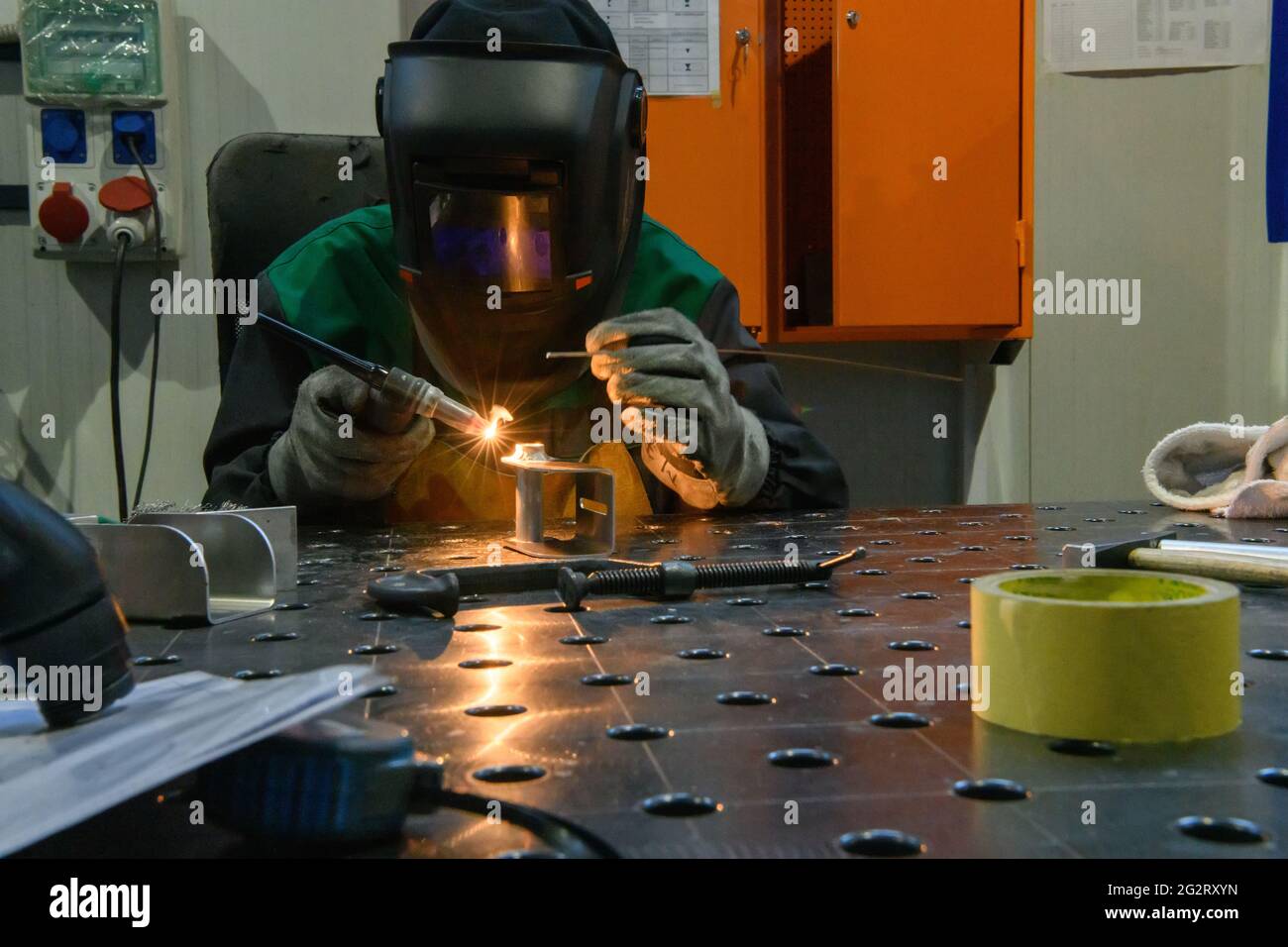 Professional welder performs work with metal parts in factory, sparks ...