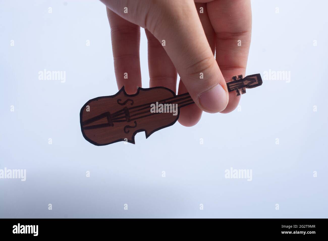 Closeup of a male holding a small wooden miniature violin on a white ...