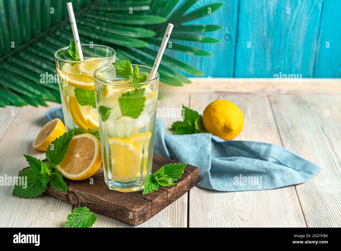 Cool lemonade with ice and mint on a blue background with palm leaves ...