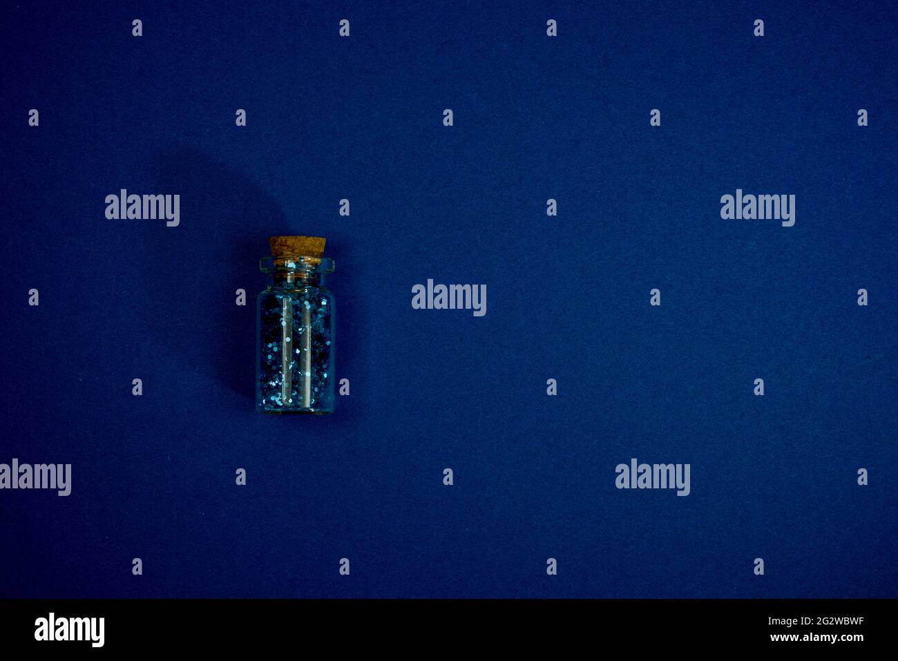 A small, mysterious glass vial with magical powder in it on a dark blue ...