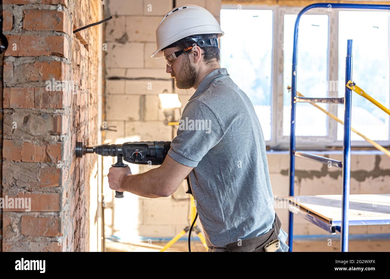 Handyman at a construction site in the process of drilling a wall with ...
