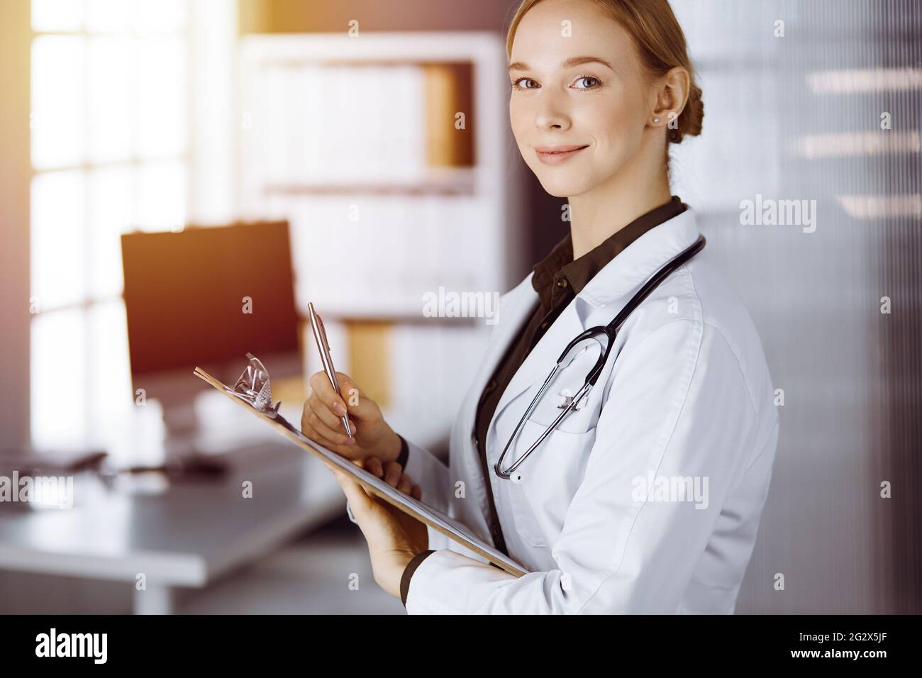 Cheerful smiling female doctor using clipboard in clinic. Portrait of ...