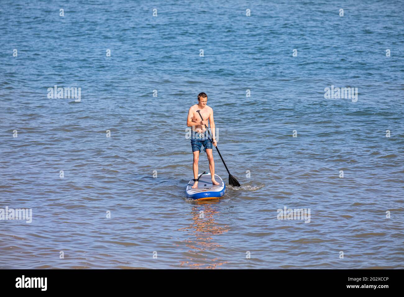 A young man paddle boarding on a calm blue sea Stock Photo - Alamy