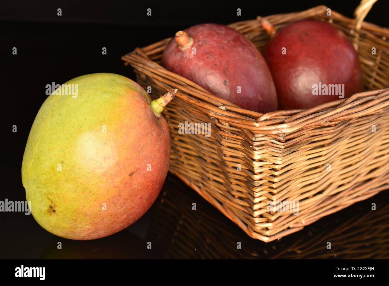 Three ripe organic mangoes on a ceramic plate, close-up, on a black ...