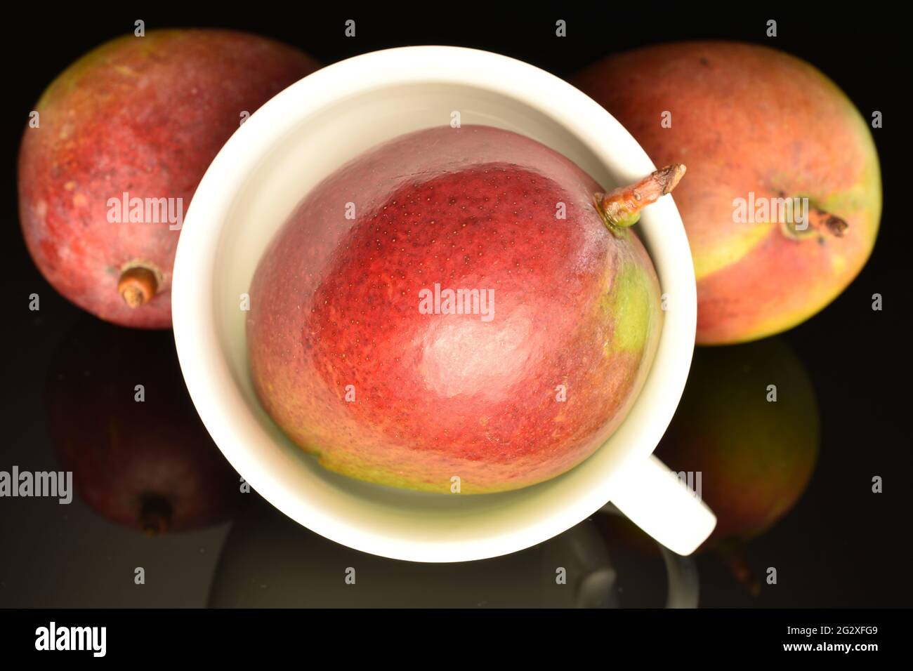 Three ripe organic mangoes with a cup, close-up, on a black background ...