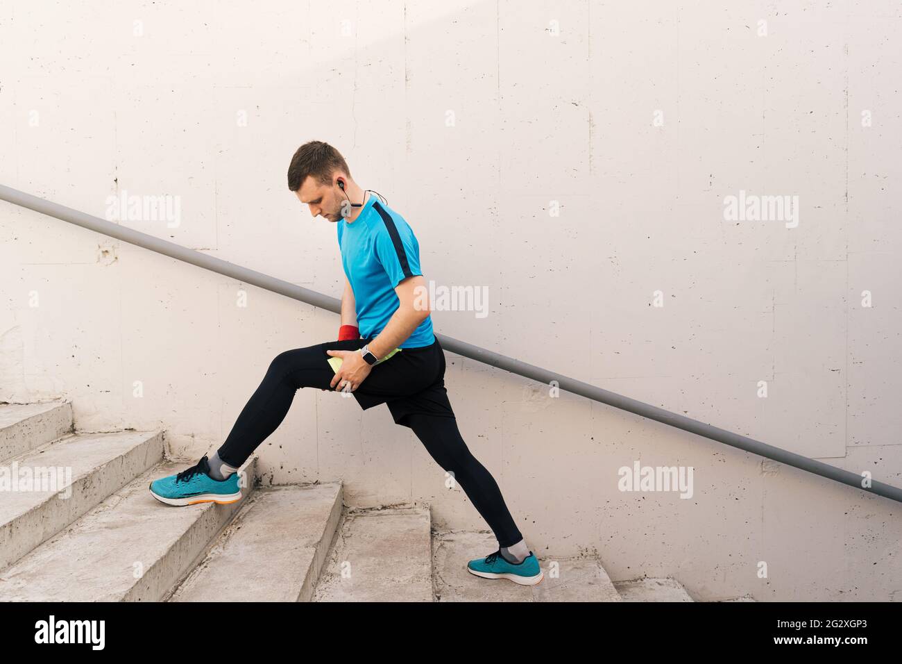 Young man runner getting ready to run stretching legs warm up quad ...