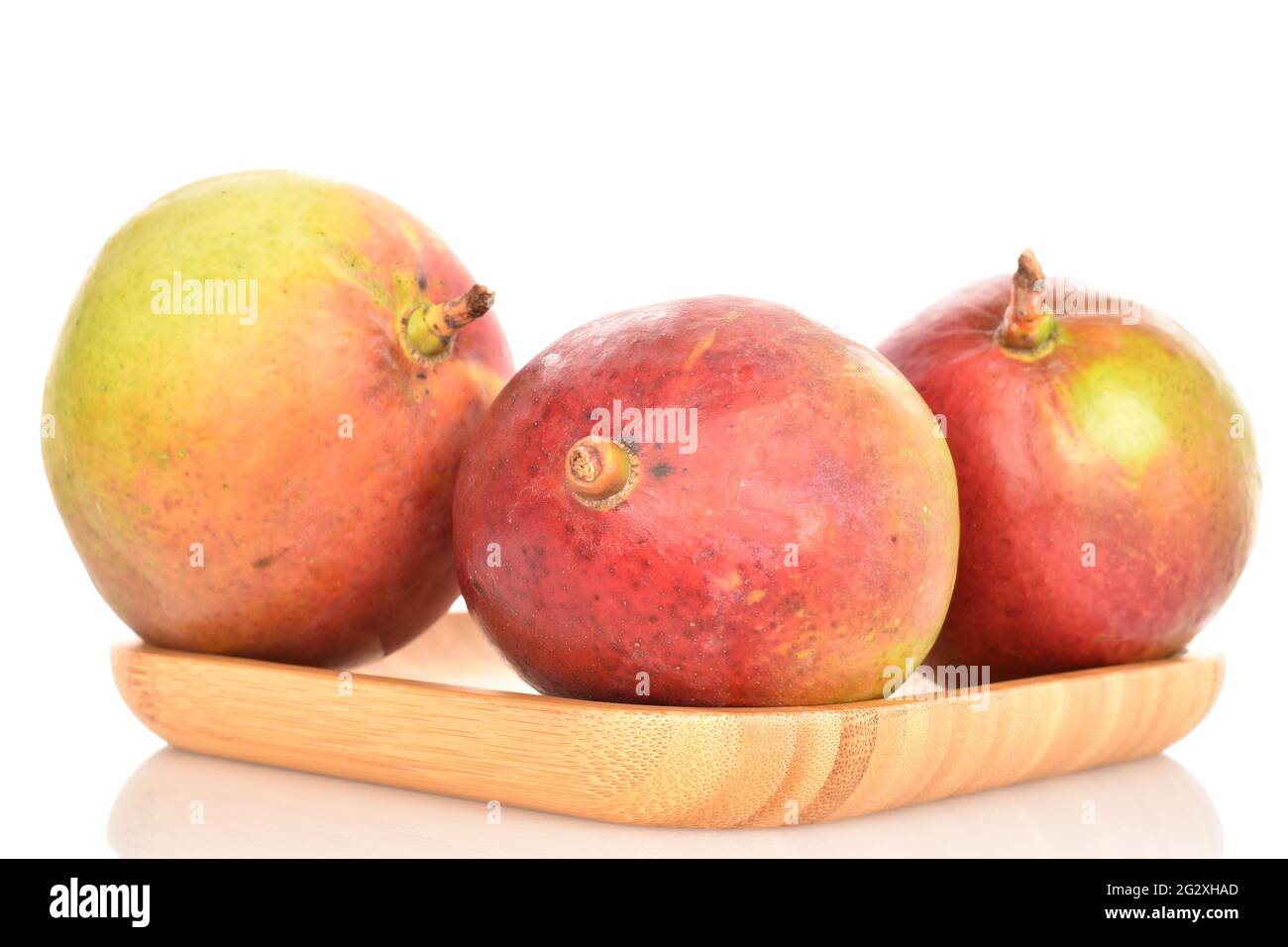 Three ripe mangoes on a bamboo plate, close-up, on a white background ...