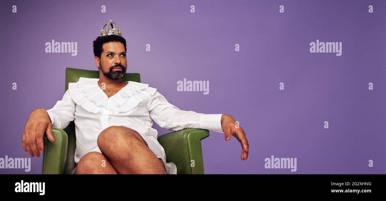 Attractive drag queen sitting on arm chair and looking away. Man with ...
