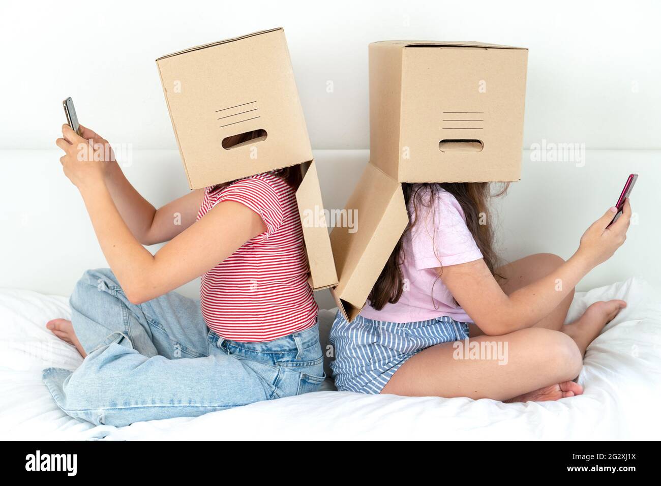Two teenage girls with boxes on their heads are sitting and looking at ...