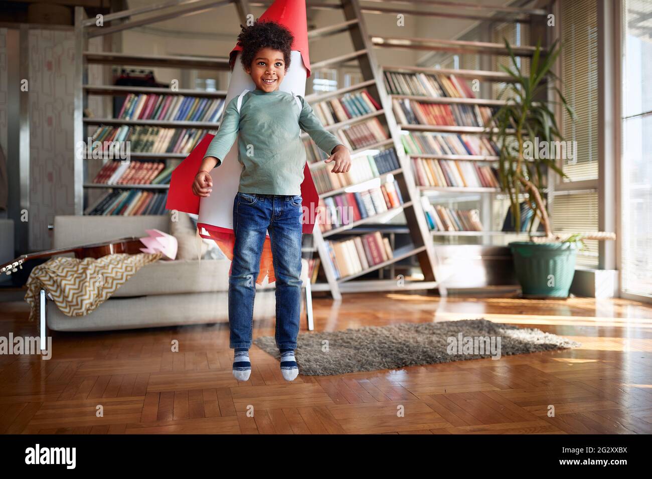A little boy with a rocket toy on his back is jumping while playing in ...