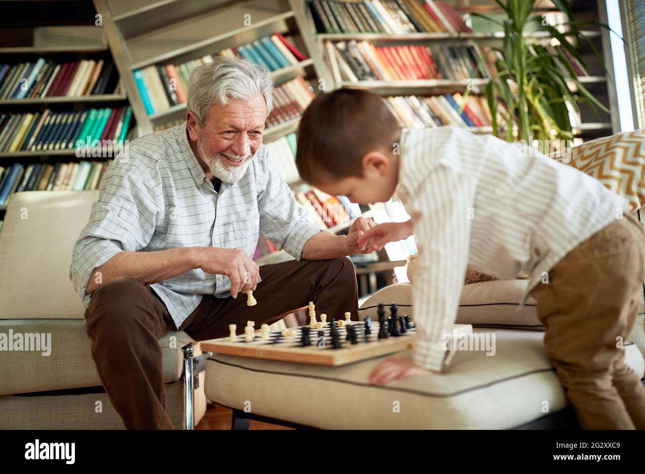 A cheerful Grandpa is playing the chess with his little grandson and ...