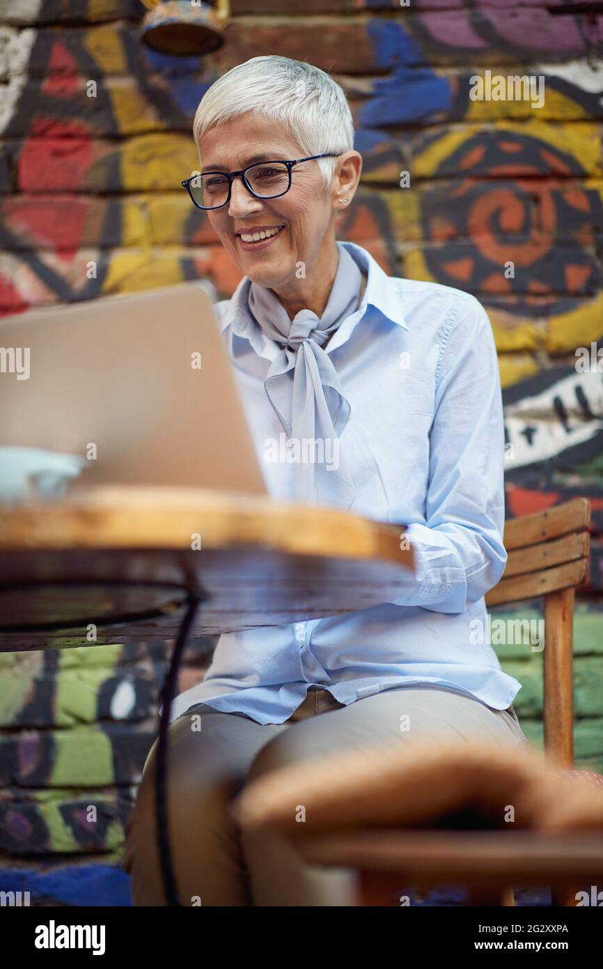 elderly female sitting at the table looking at her laptop in outdoor ...