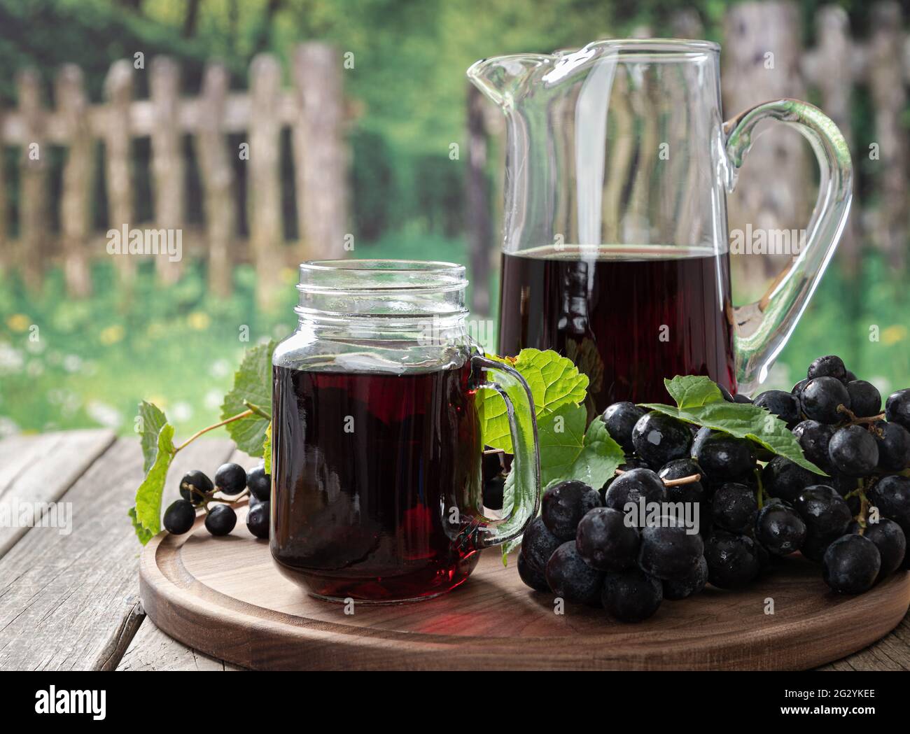 Glass of grape juice with fresh grapes and pitcher on wooden tray with ...