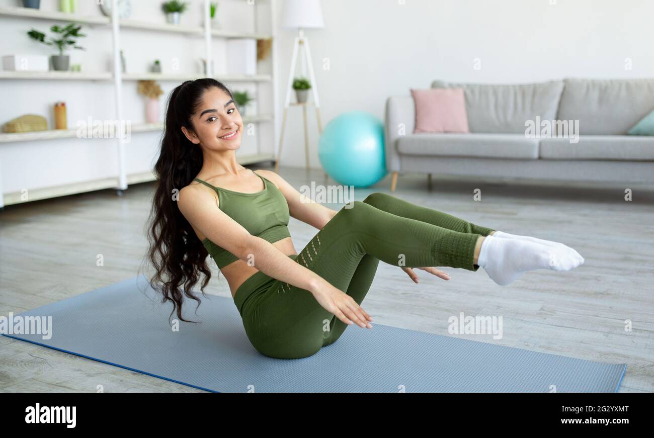 Positive athletic Indian woman doing abs exercises during her domestic ...