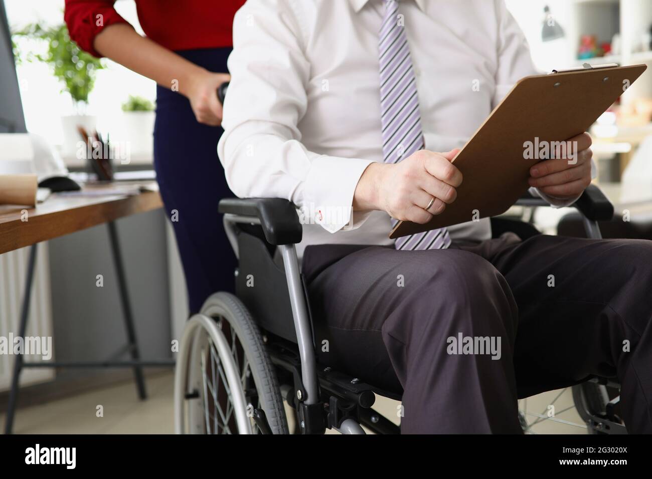 Woman secretary rolls CEO in wheelchair with documents and reports in ...