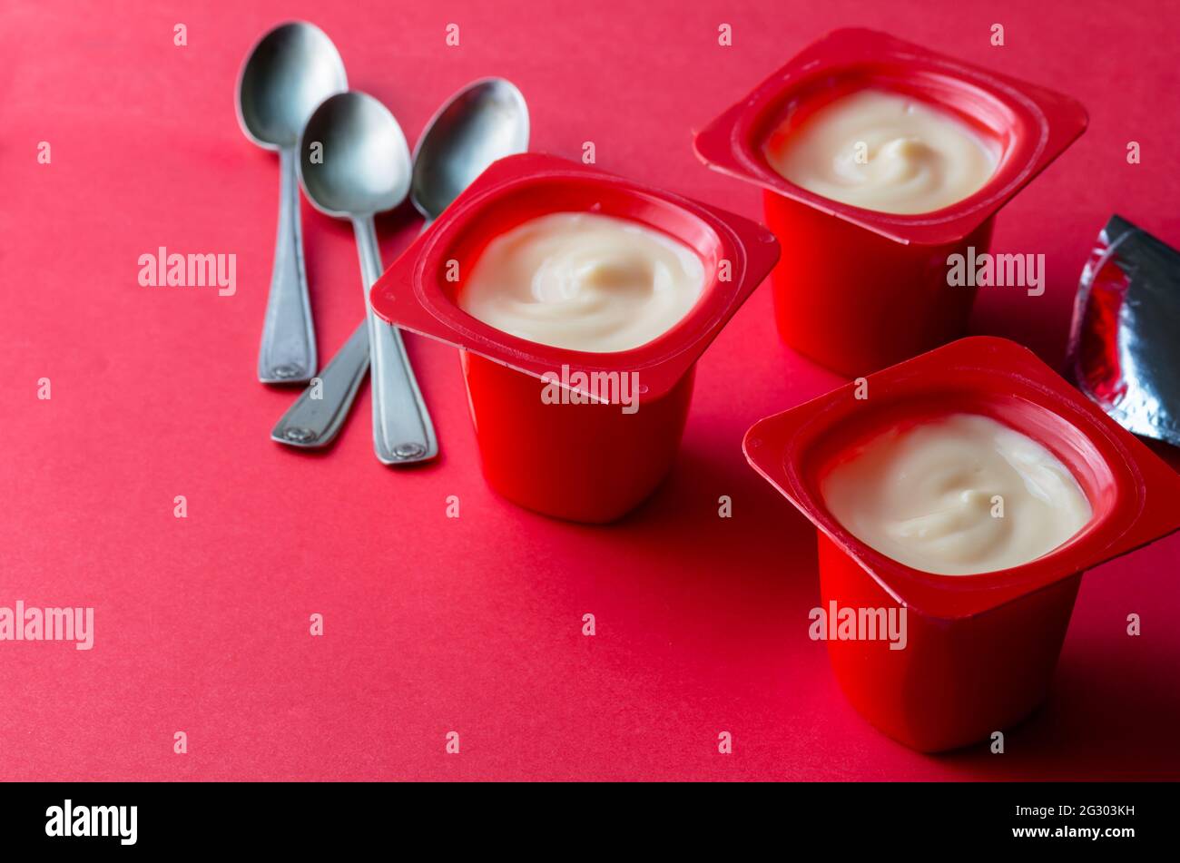 Three red yogurt plastic pots with spoons and foil on red background ...