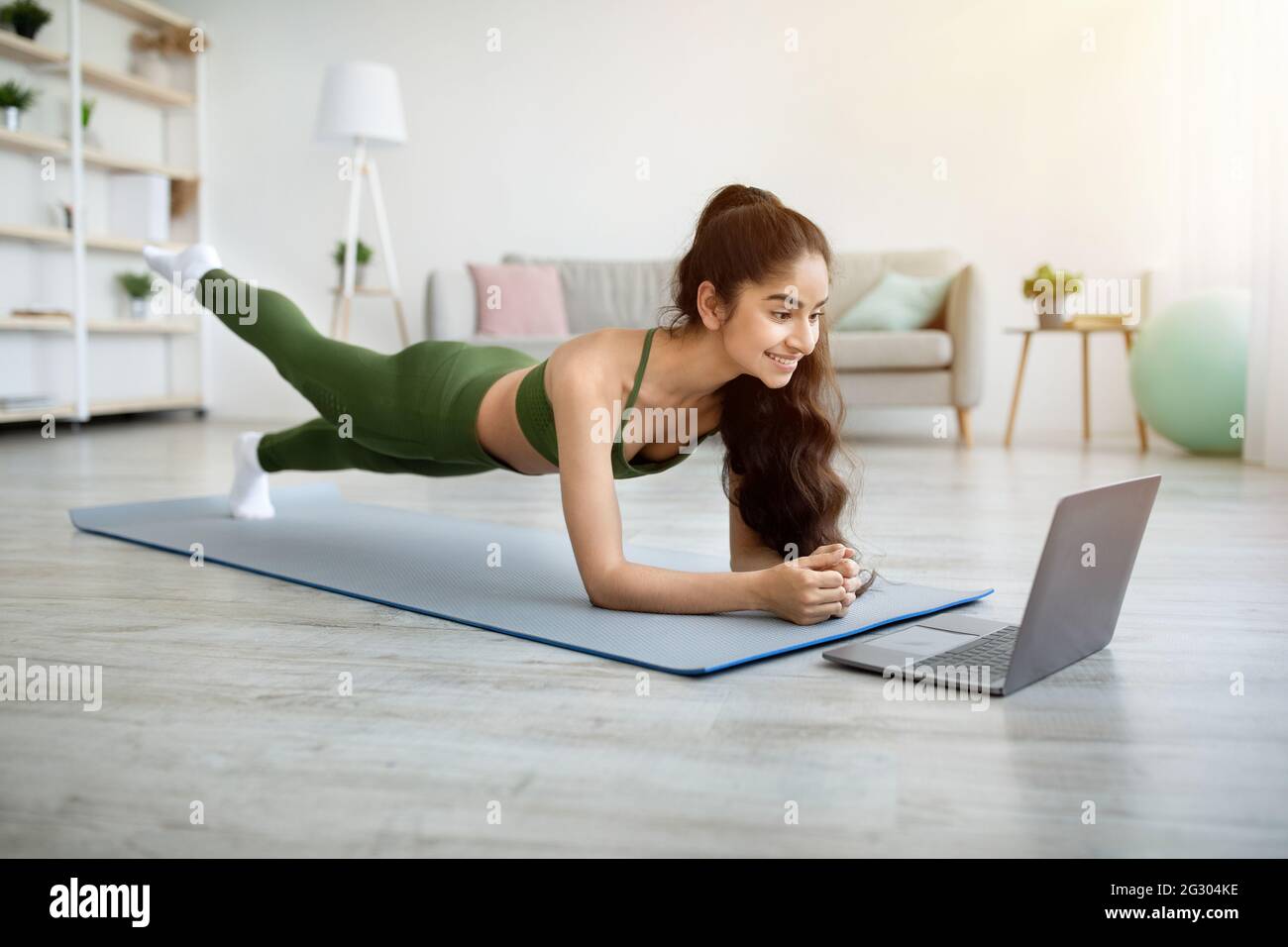 Strong Indian woman standing in elbow plank, lifting her leg on sports ...