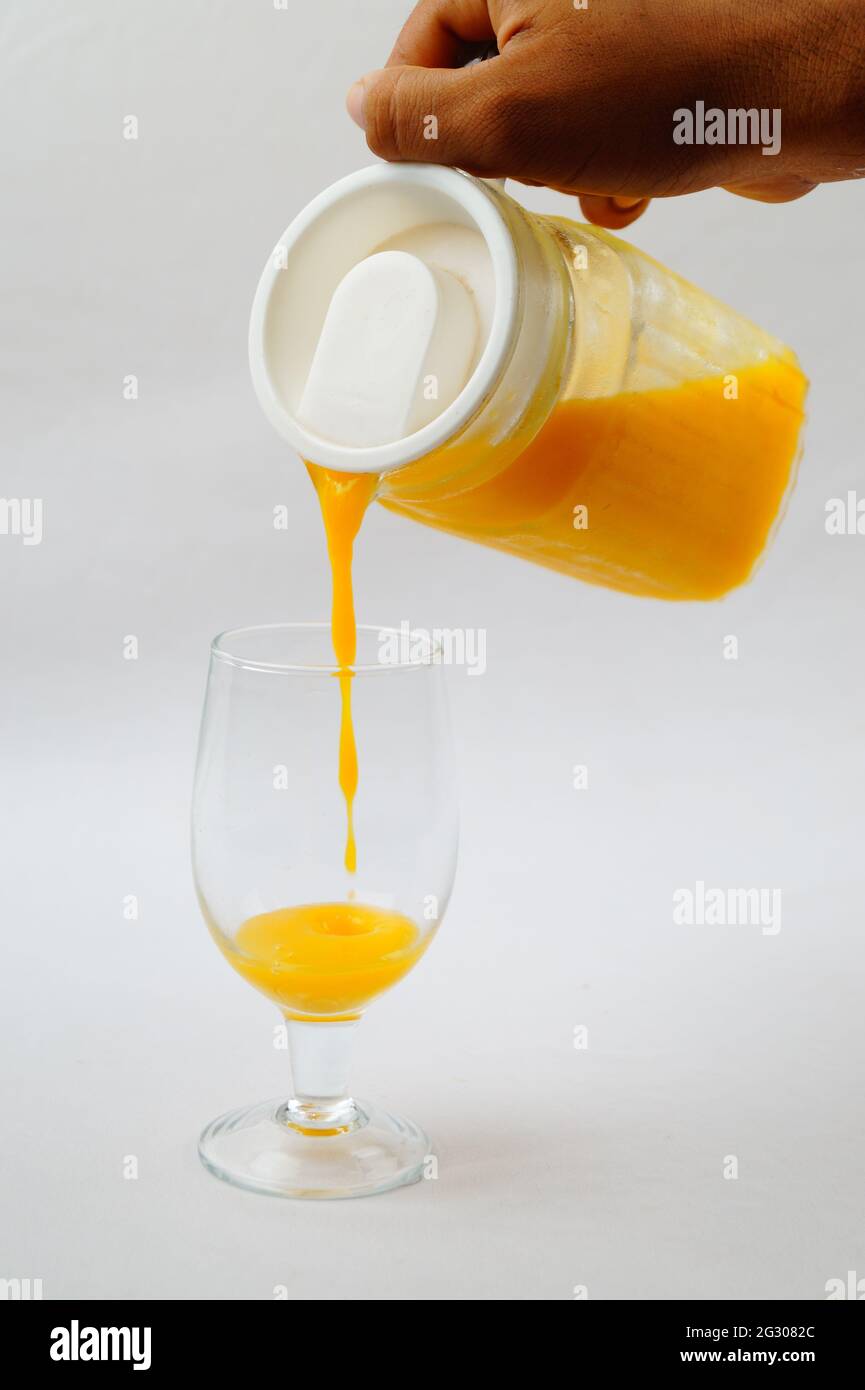 A closeup shot of a person pouring fresh mango juice into a glass on a ...