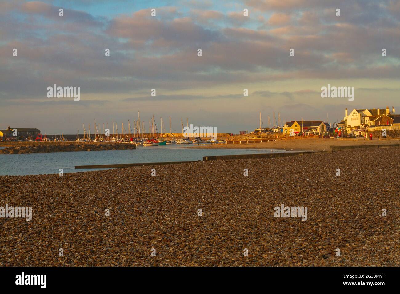 View of The Cobb Harbour at sunset from the beach at Lyme Regis in ...