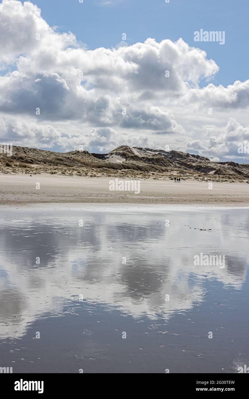 Water on the beach with mirror reflection of white clouds and dunes in ...