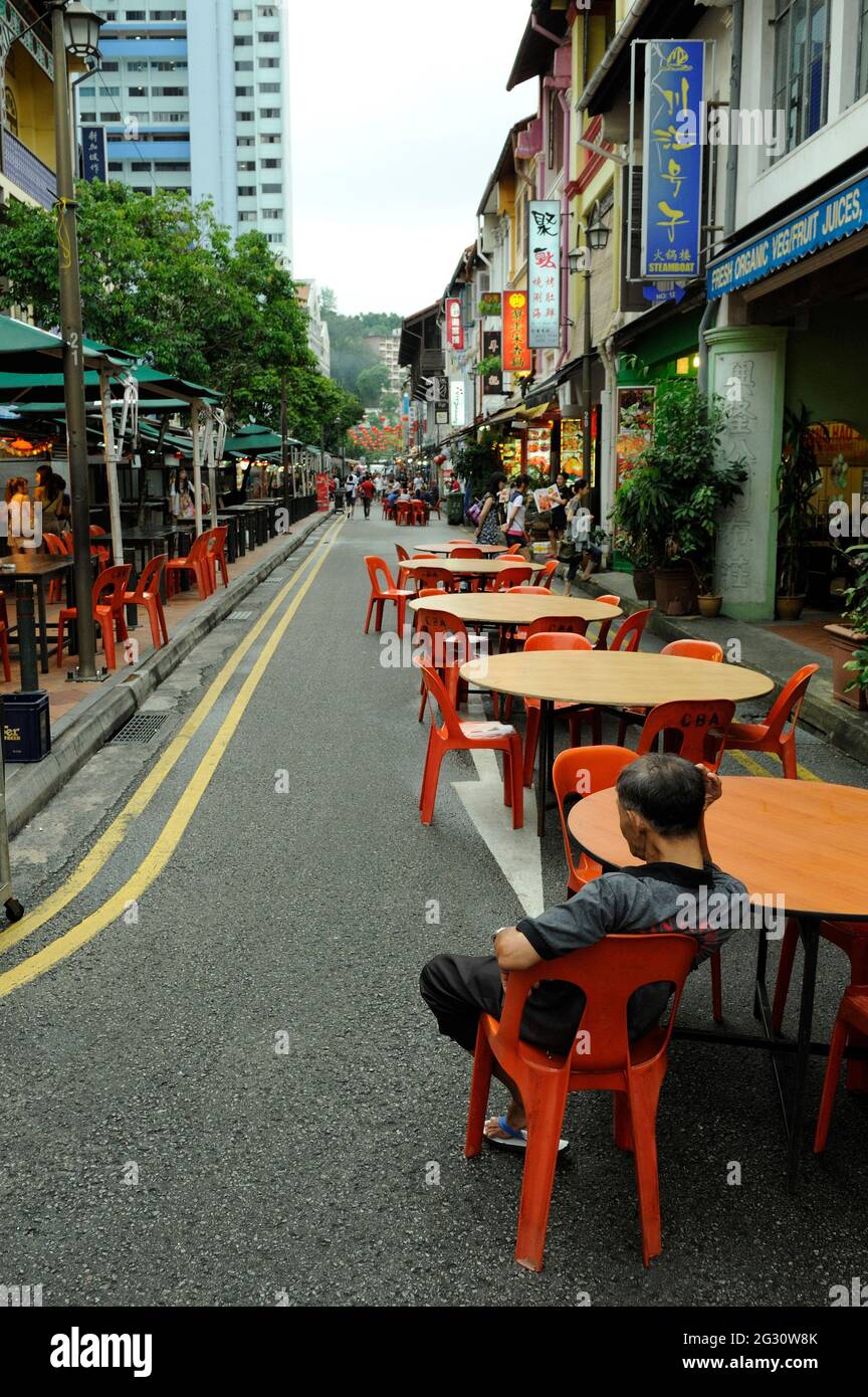Man sitting at end of long line of tables stretching down narrow street ...