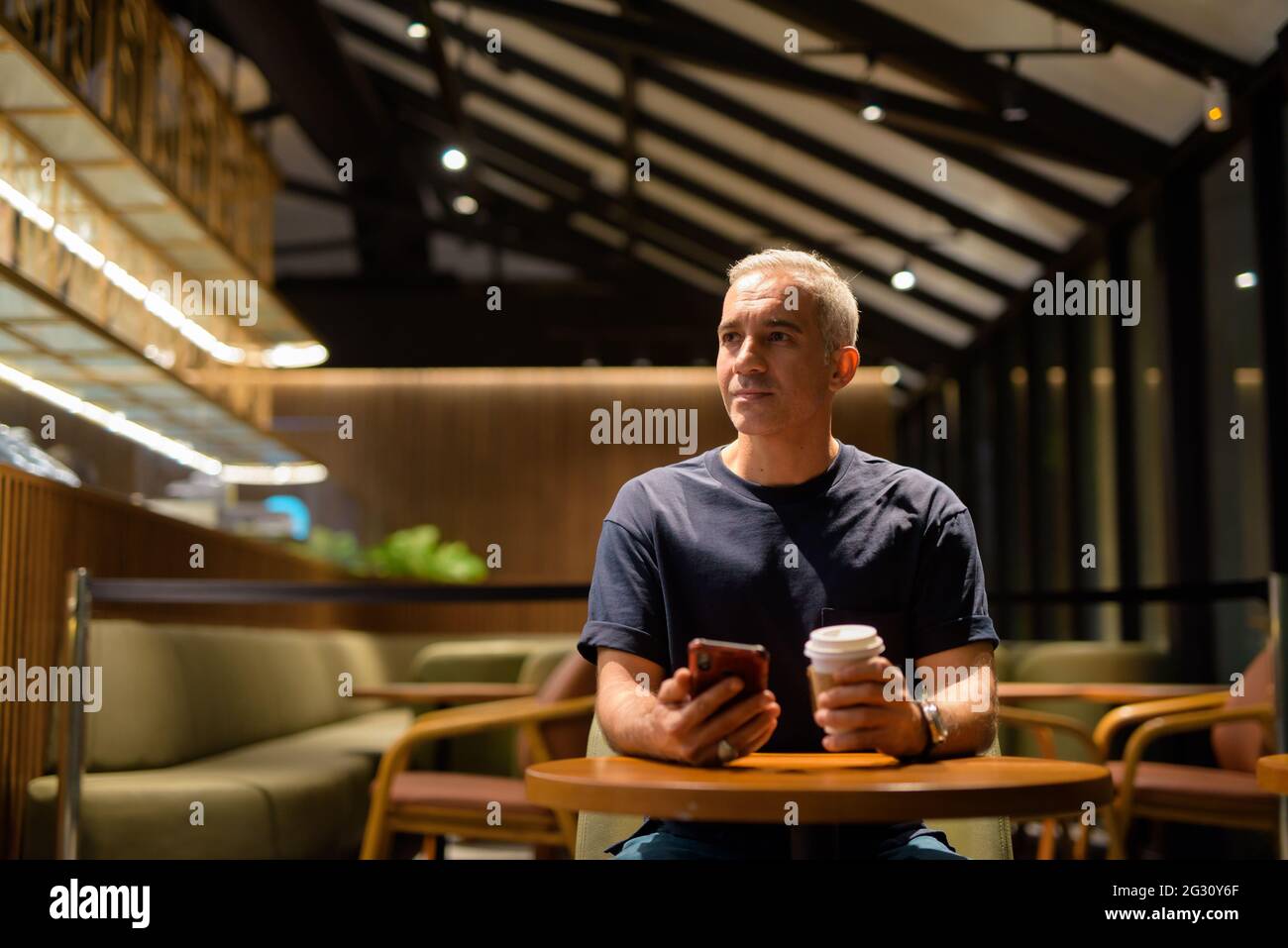 Portrait of man inside coffee shop at night thinking and using phone ...