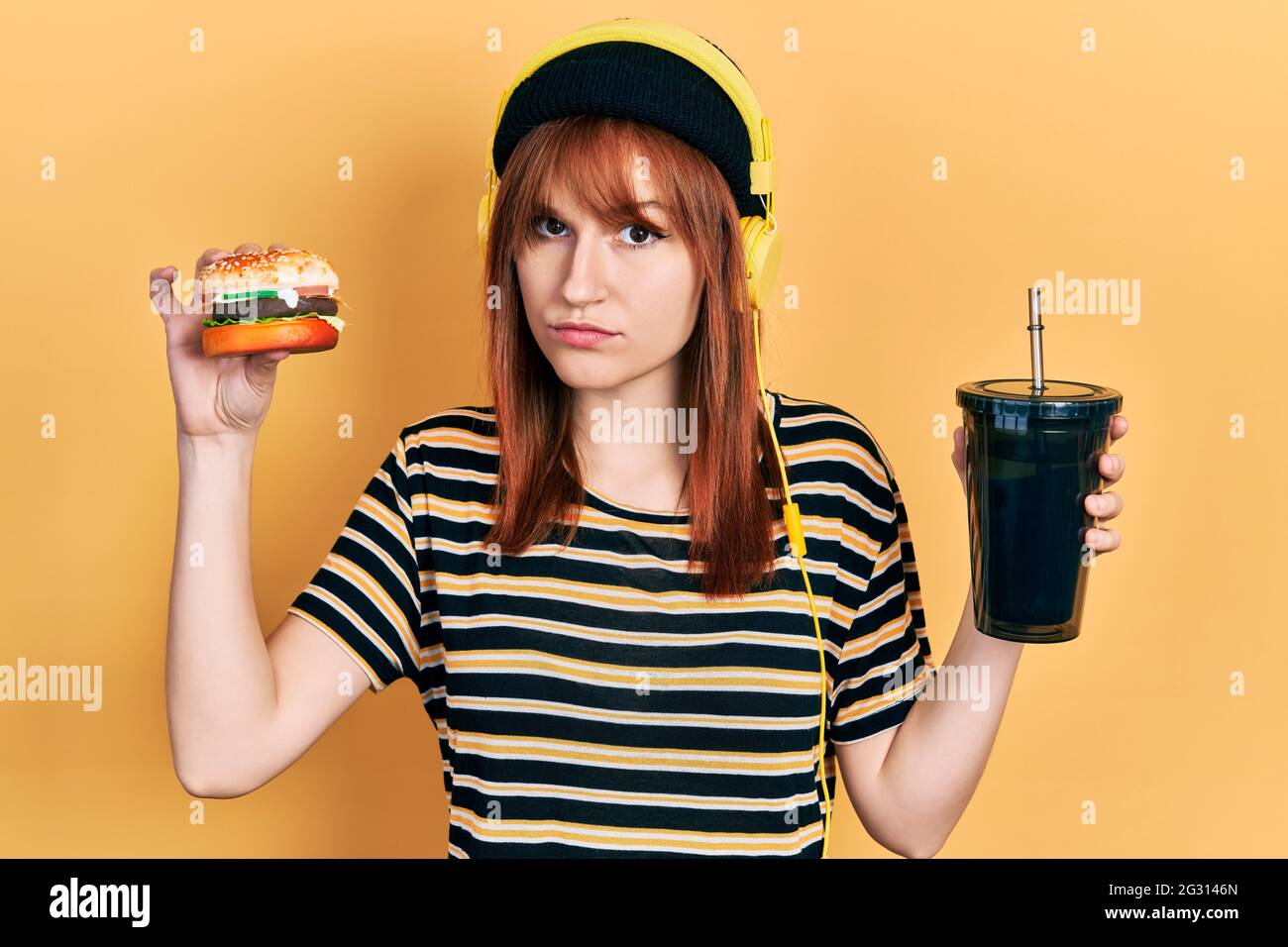 Redhead young woman eating a burger and drinking soda wearing ...