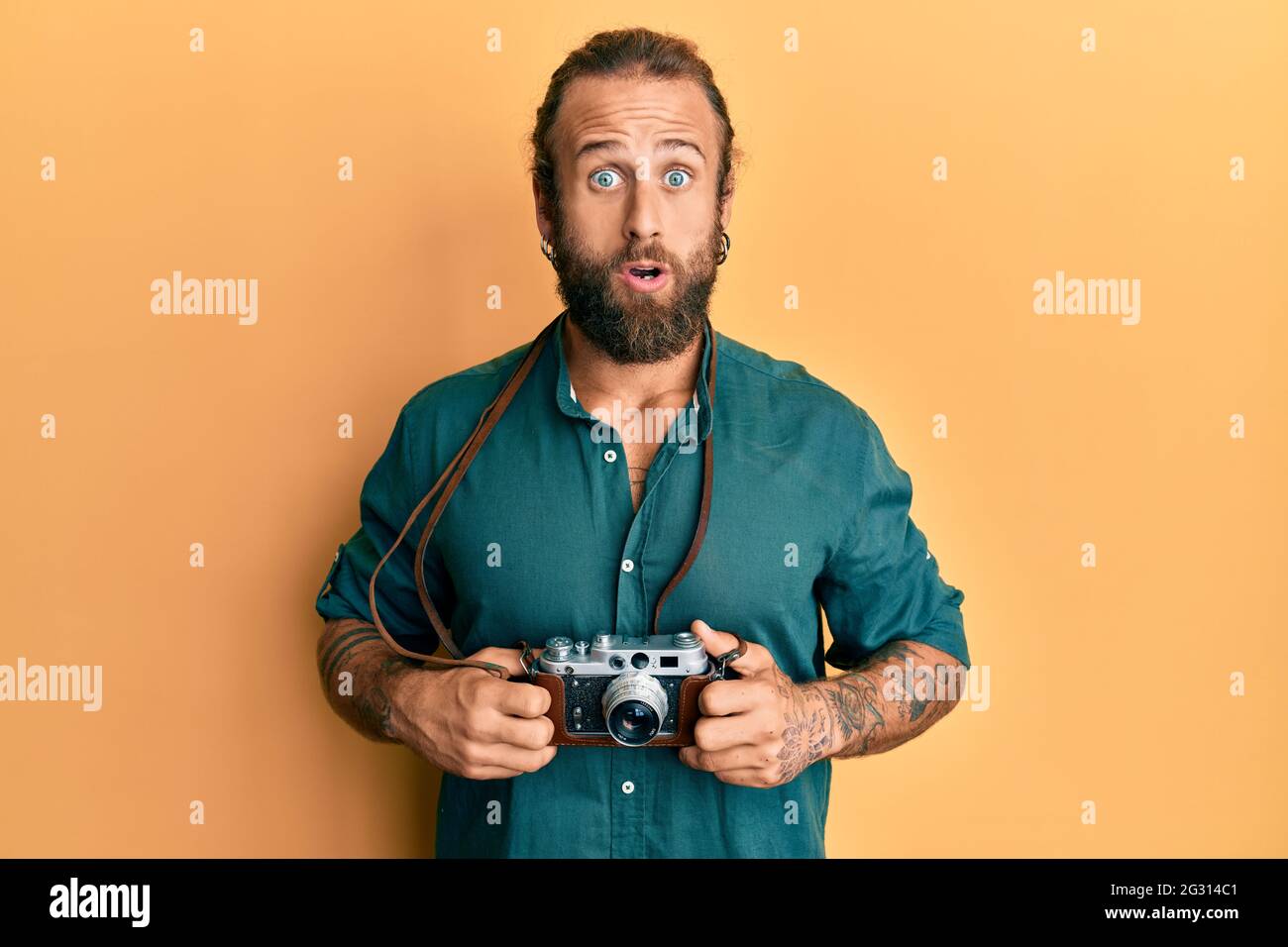 Handsome man with beard and long hair holding vintage camera in shock ...