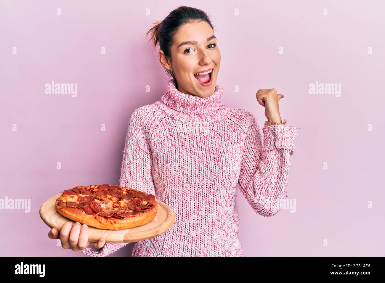 Young caucasian woman holding italian pizza pointing thumb up to the ...