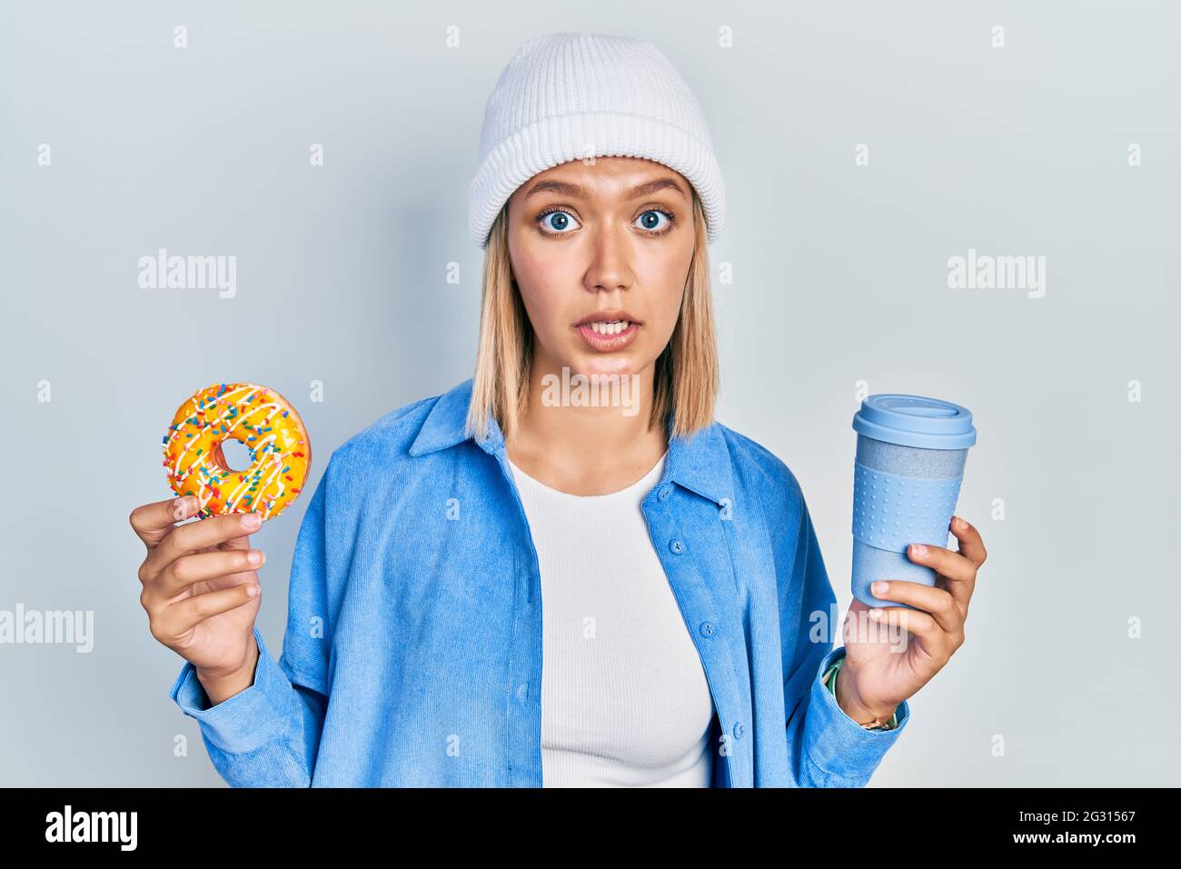 Beautiful blonde woman eating doughnut and drinking coffee clueless and ...