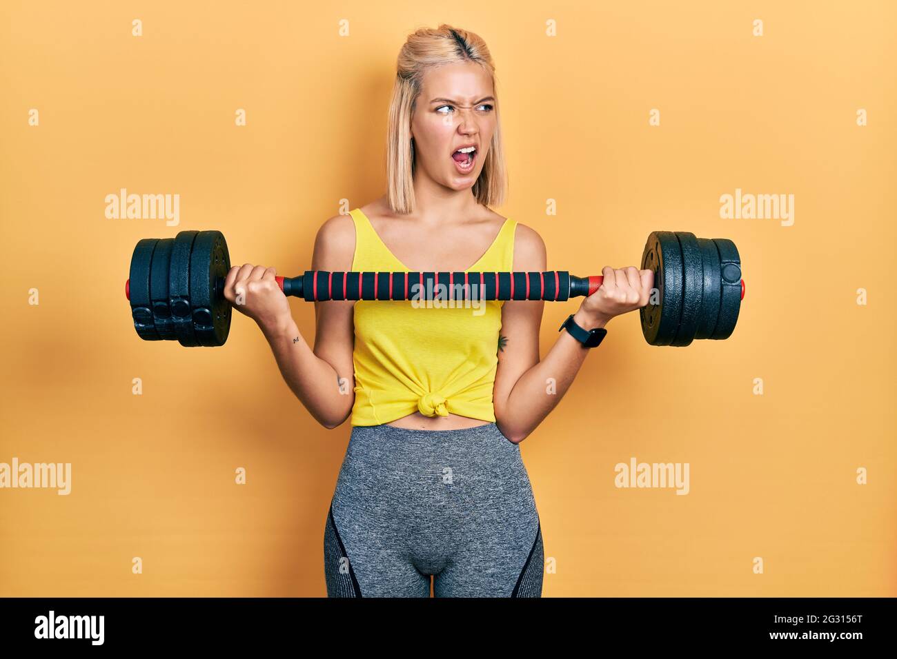 Beautiful blonde woman wearing sportswear using dumbbells angry and mad ...