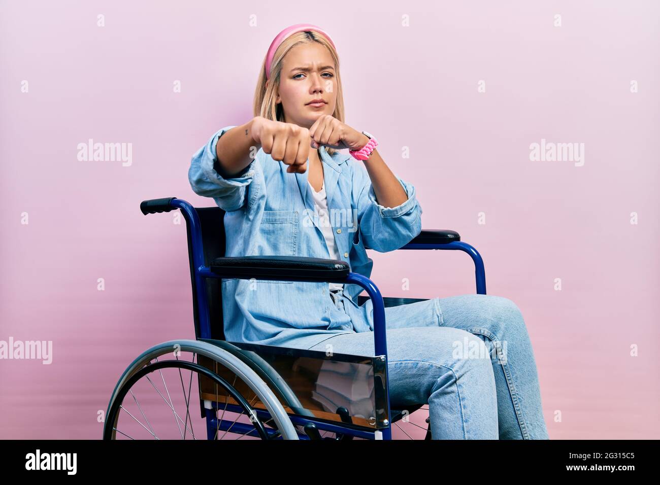 Beautiful blonde woman sitting on wheelchair punching fist to fight ...