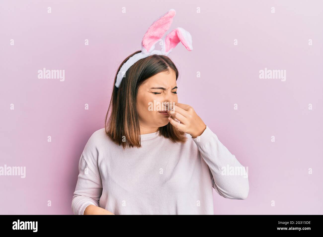 Young beautiful woman wearing cute easter bunny ears smelling something ...