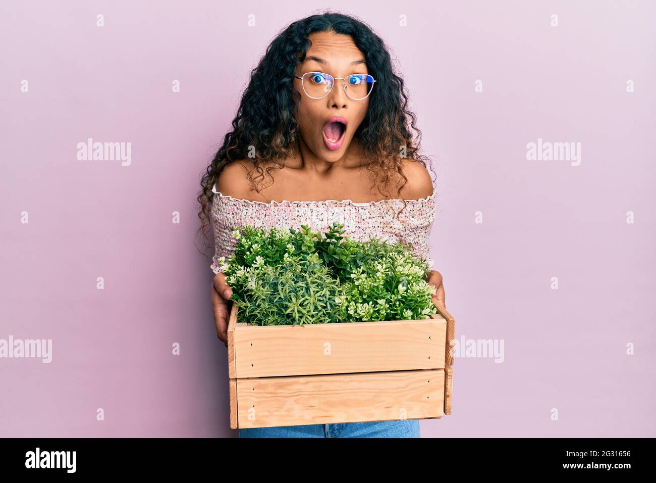 Young latin woman holding wooden plant pot afraid and shocked with ...