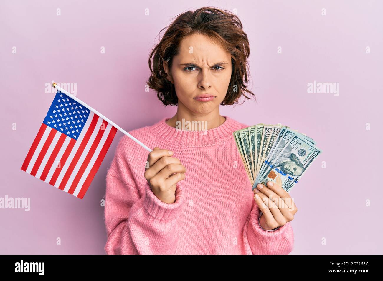 Young brunette woman holding united states flag and dollars depressed ...