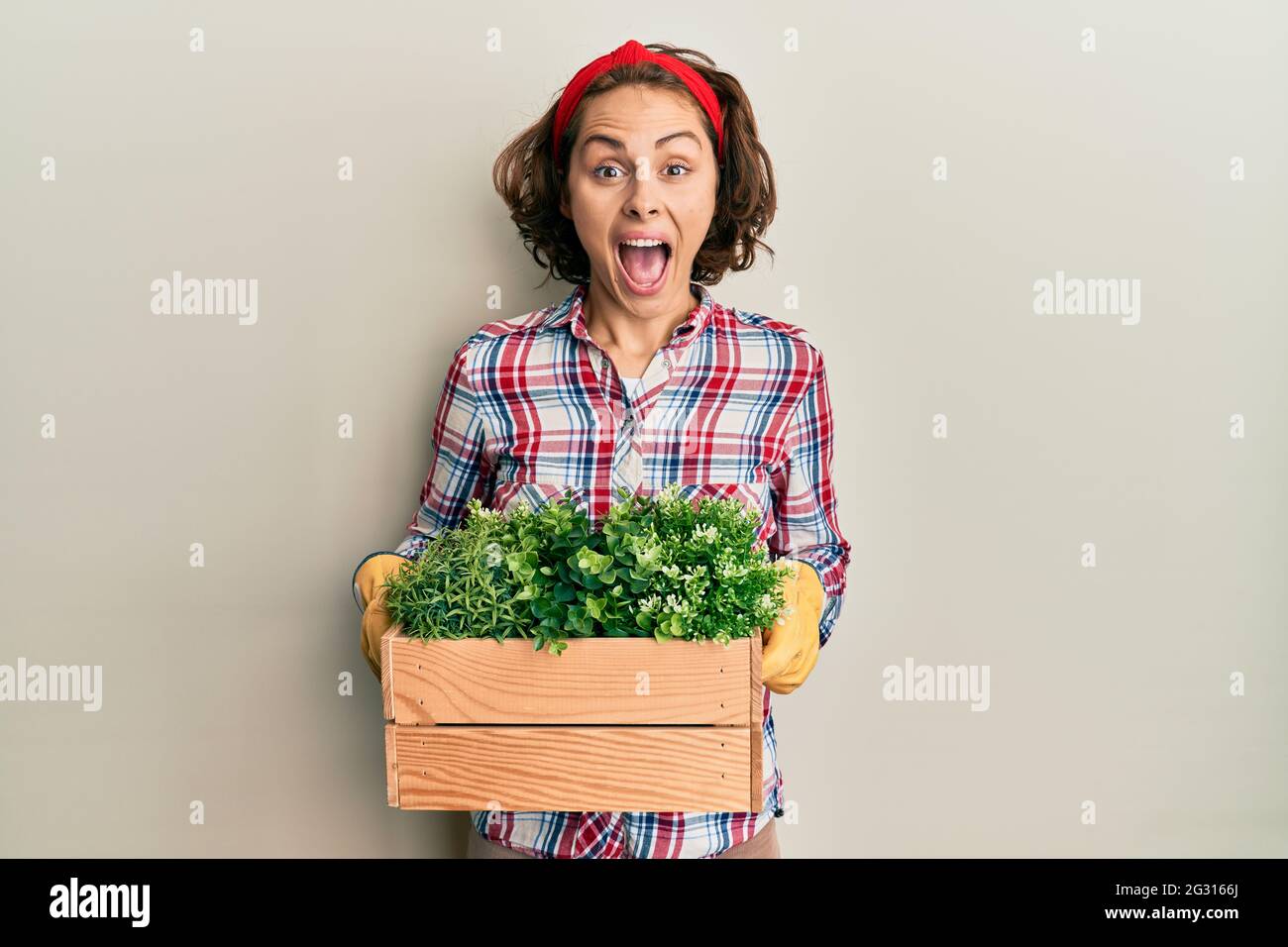 Young brunette woman wearing gardener clothes holding wooden plant pot ...