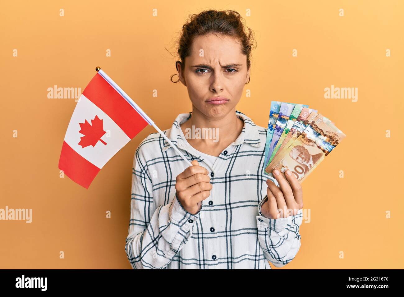 Young brunette woman holding canada flag and dollars depressed and ...