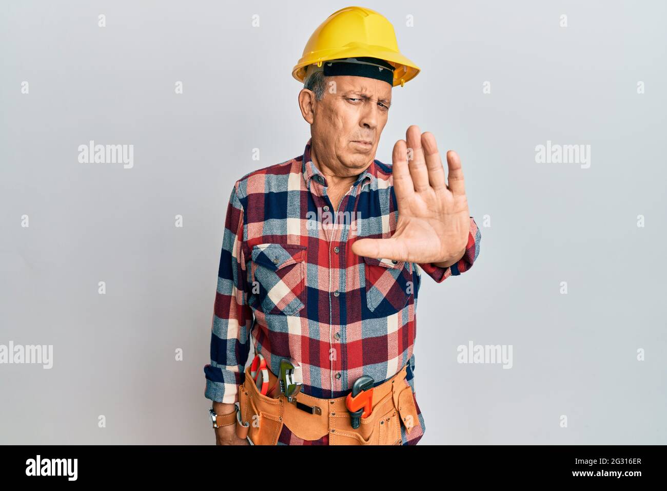 Senior hispanic man wearing handyman uniform doing stop sing with palm ...
