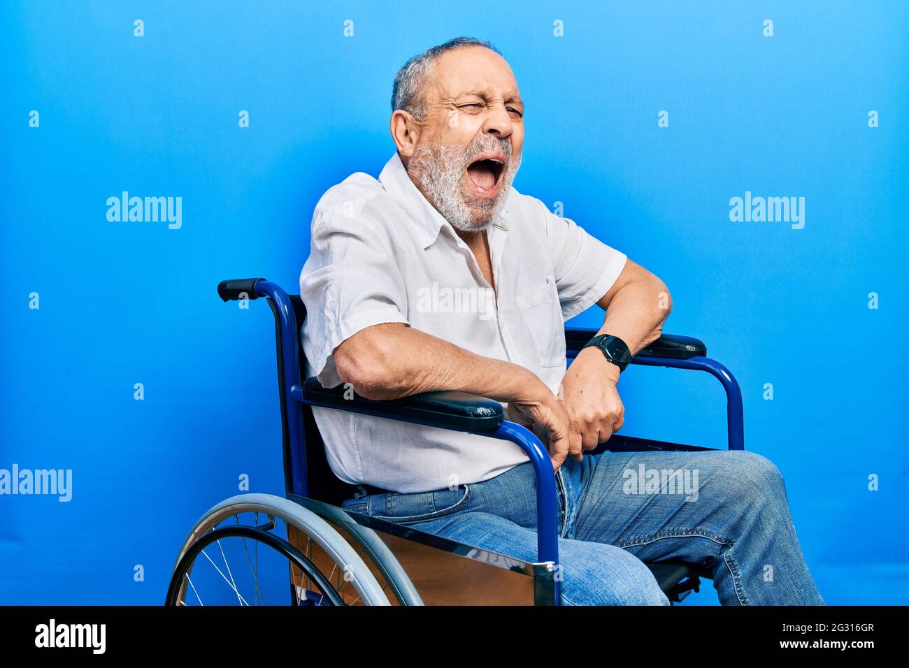 Handsome senior man with beard sitting on wheelchair angry and mad ...