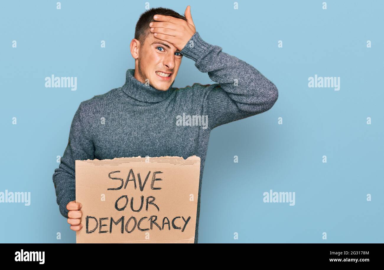 Young blond man holding save our democracy protest banner stressed and ...