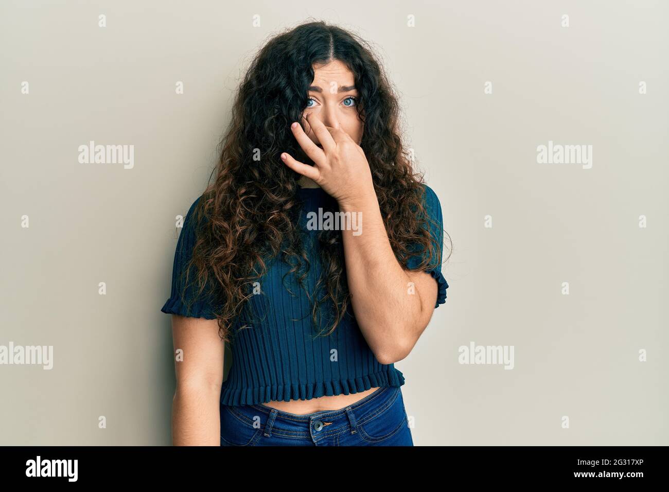 Young brunette woman with curly hair wearing casual clothes smelling ...