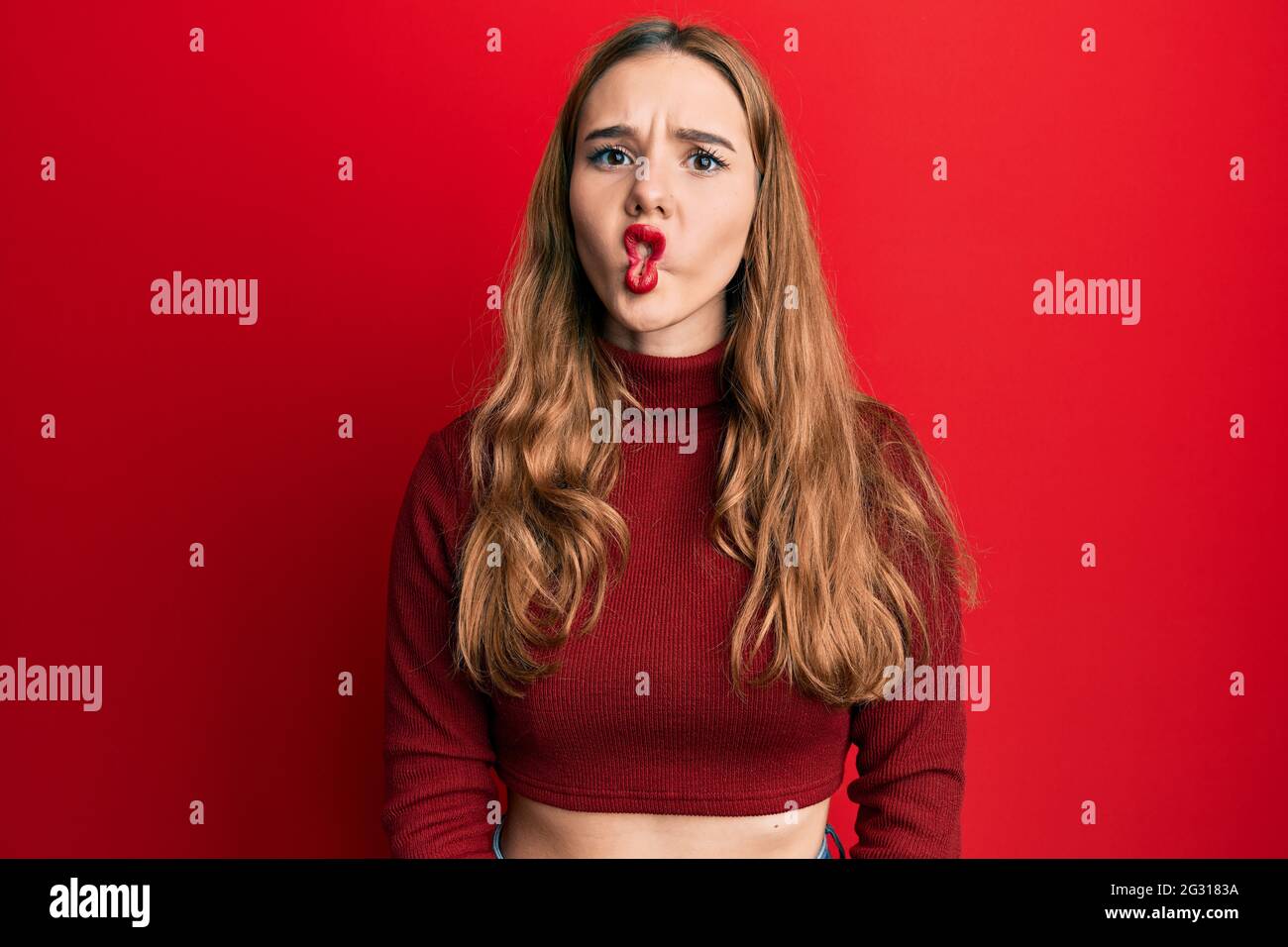 Young blonde woman wearing turtleneck sweater making fish face with ...