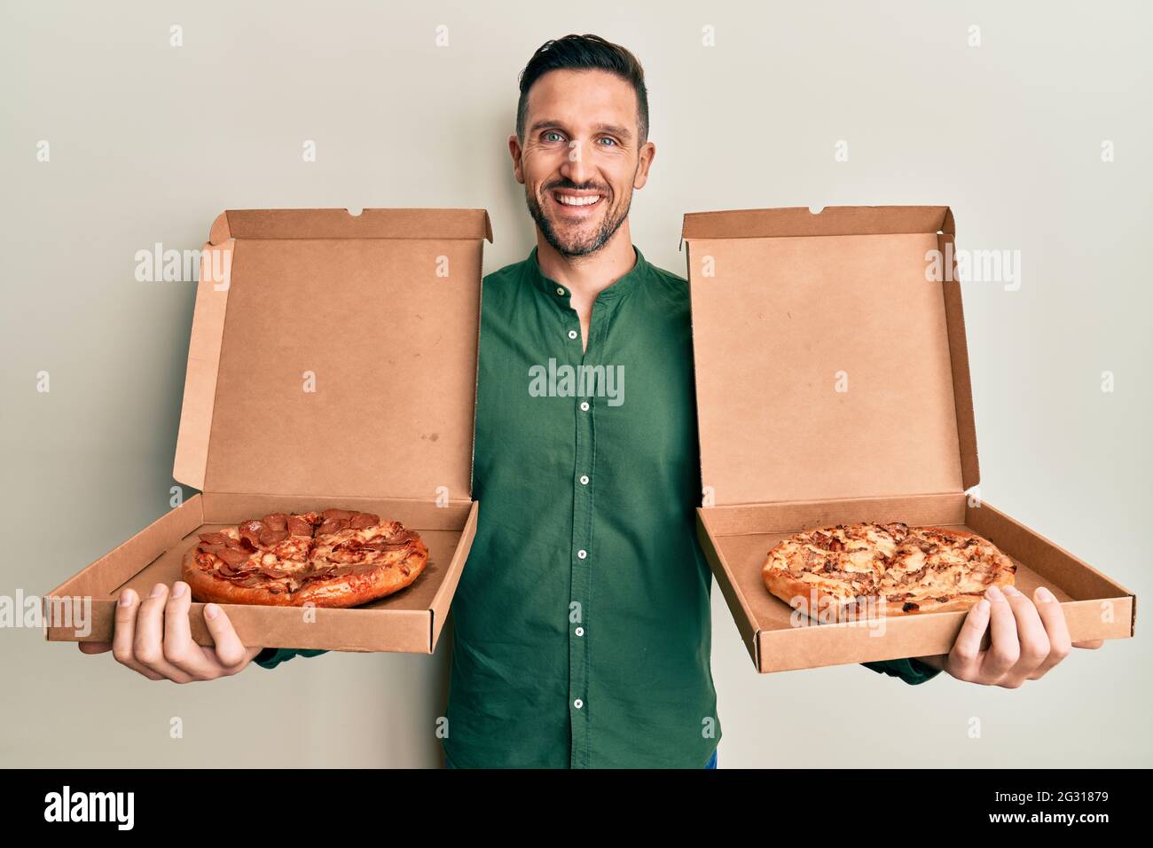 Handsome man with beard holding two italian pizzas smiling with a happy ...