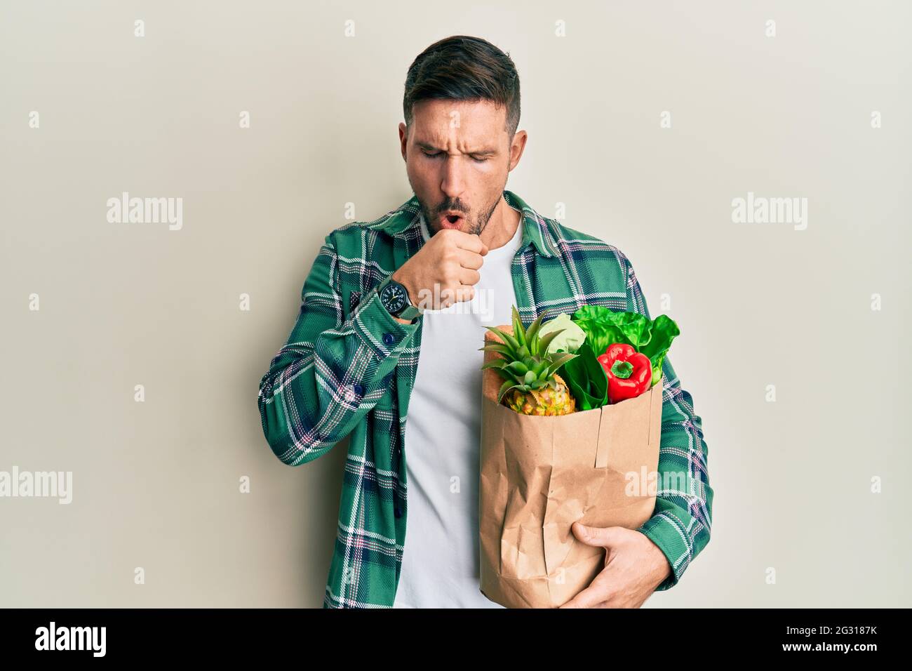 Handsome man with beard holding paper bag with groceries feeling unwell ...