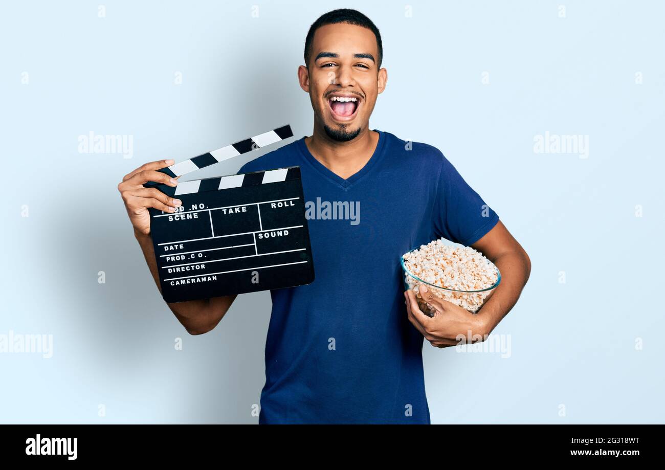 Young african american man eating popcorn holding film clapboard ...