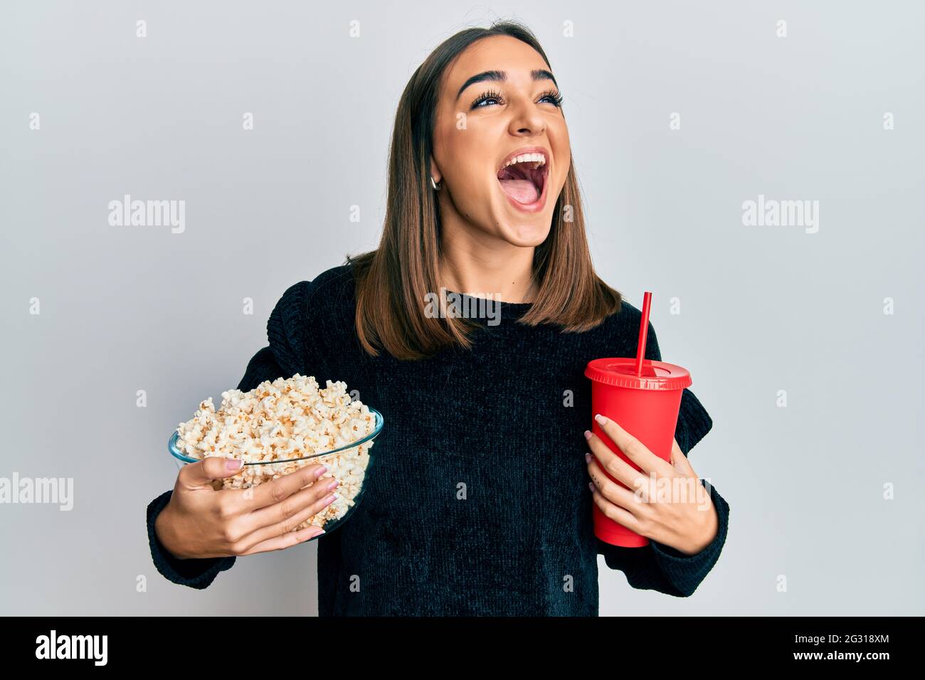 Young brunette girl eating popcorn and drinking soda angry and mad ...