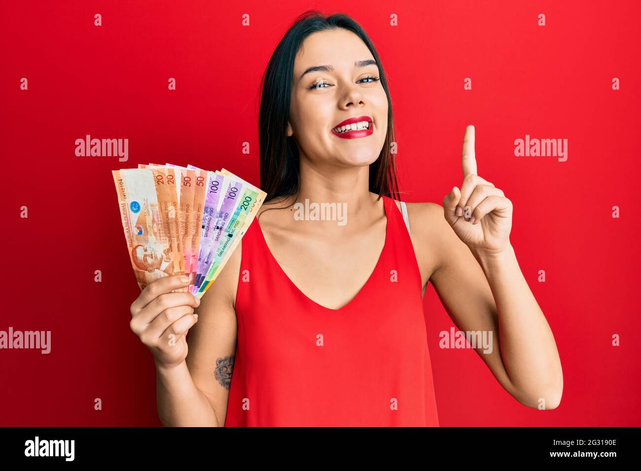 Young hispanic girl holding philippine peso banknotes smiling with an ...