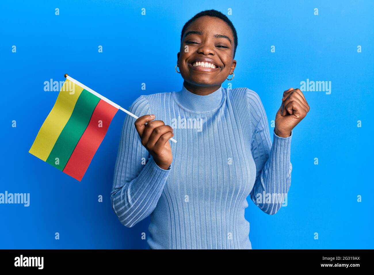 Young african american woman holding lithuania flag screaming proud ...