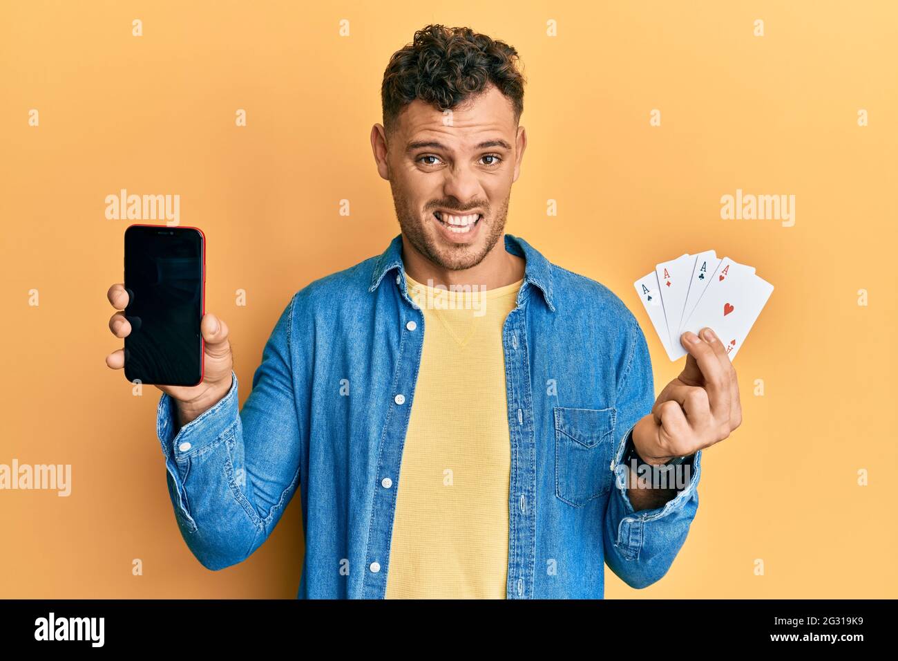 Young hispanic man holding poker cards and smartphone showing blank ...