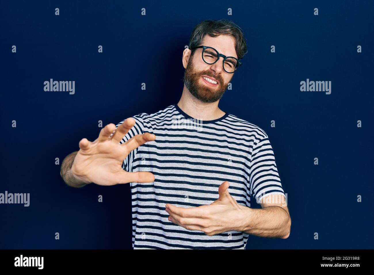 Caucasian man with beard wearing striped t shirt and glasses disgusted ...